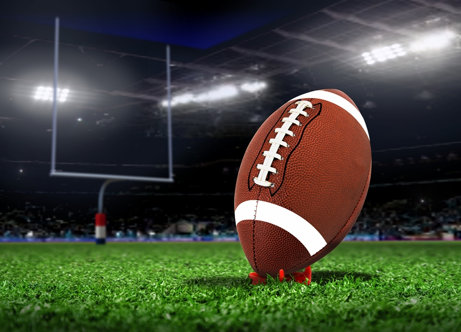 A football is sitting on the field in front of a stadium. – Do It ...
